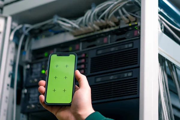 Data center close-up hacker or engineer holding phone with green screen ...