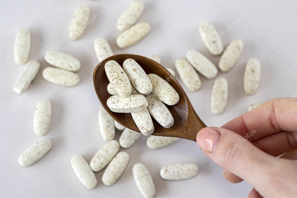 A full wooden spoon of oval beige tablets with speckles on a beige ...