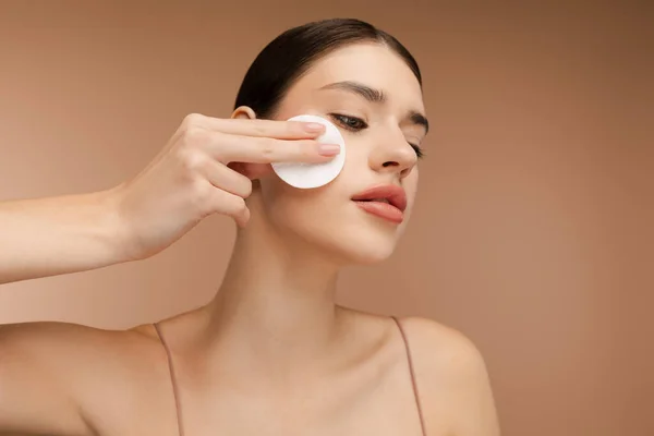 Portrait of young lady taking off makeup with cotton sponge while ...