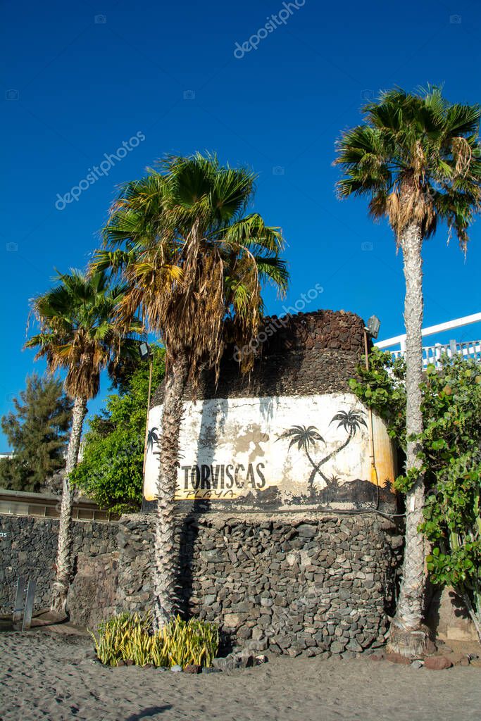 Torviscas Playa lettering on a stone wall on the beach, with palm trees ...