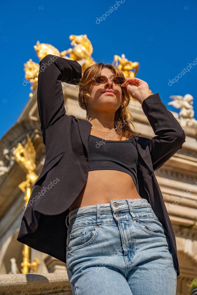 Hermosa joven modelo con el pelo largo y rubio en jeans azules, tocando sus gafas de sol, la ...