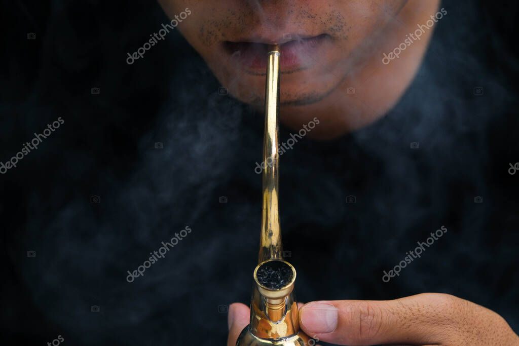 "Asian man smokes marijuana from a pipe at home. Studio shoot with ...