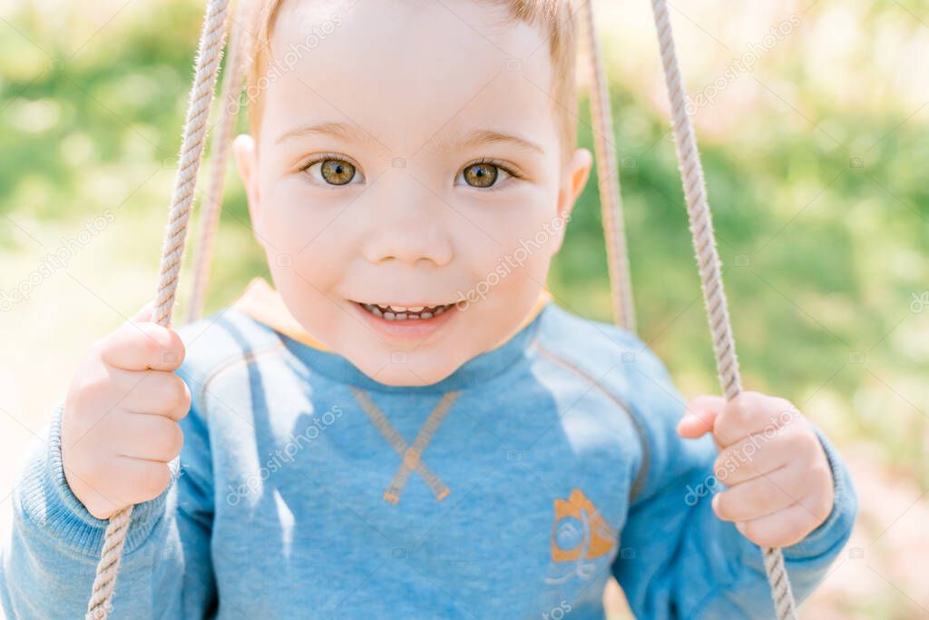 Feliz niño de tres años vestido con ropa azul amarilla columpios ...