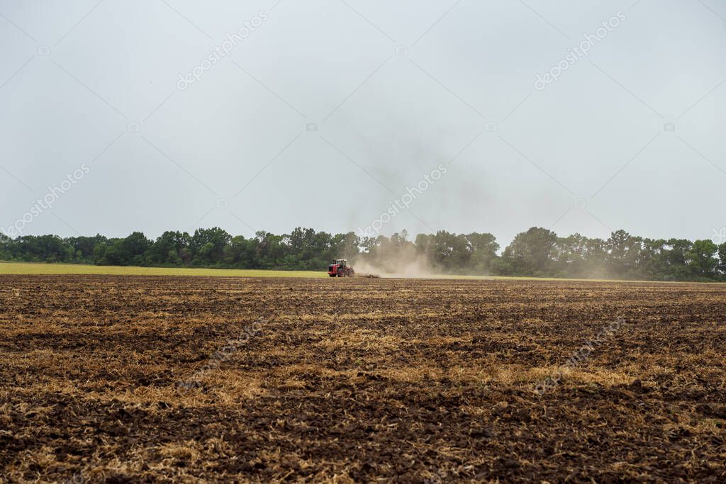A tractor is plowing a field in the dust. Harvesting with a combine ...