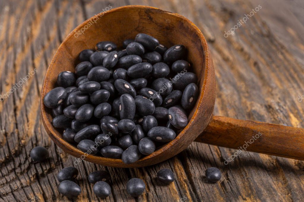 Una cuchara de madera está llena de frijoles negros brillantes que se ...