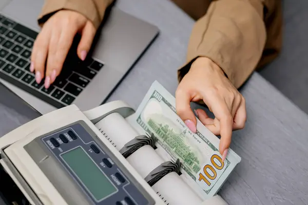 Close-up of female worker with laptop and dollar bills in electronic ...