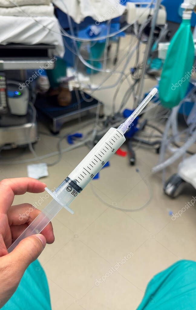 hand holds a syringe amidst IV drips and medications, symbolizing ...