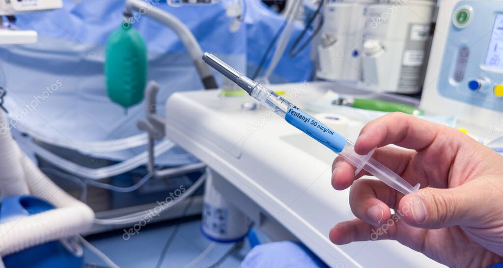 hand holds a syringe amidst IV drips and medications, symbolizing ...