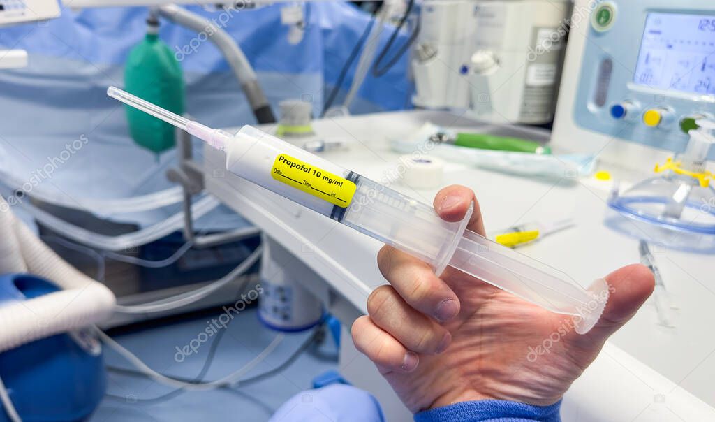 hand holds a syringe amidst IV drips and medications, symbolizing ...