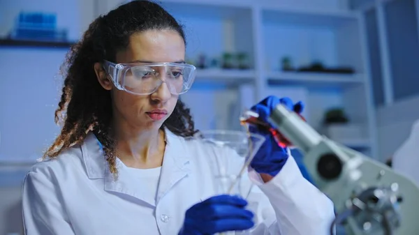 Busy female scientist in protective goggles mixing liquids, conducting ...