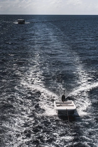In the deep blue ocean, a small fisherman's boat is tethered to an ...