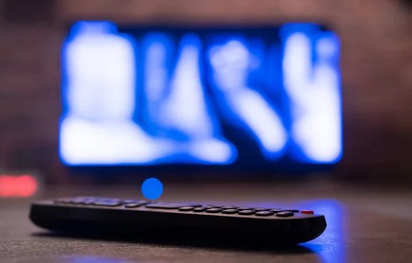 Remote control on a table with a TV on the background. shallow depth of ...