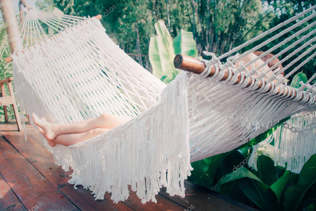 Vista trasera de la hermosa chica en una hamaca blanca en el jardín en casa. Mujer joven ...